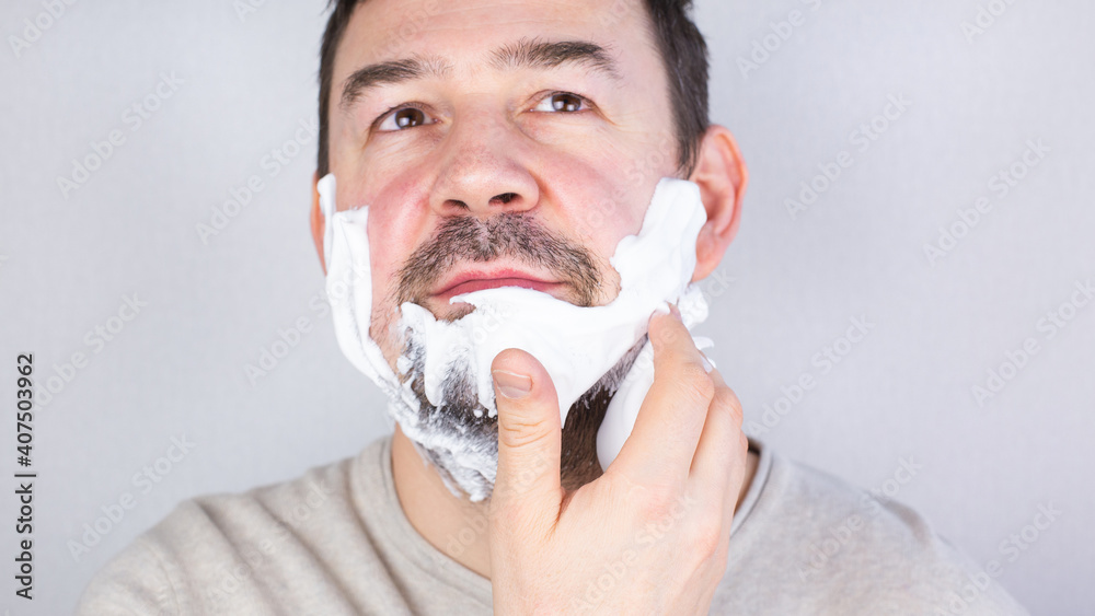 Caucasian dark-haired man applying shaving foam for his beard, looking ...