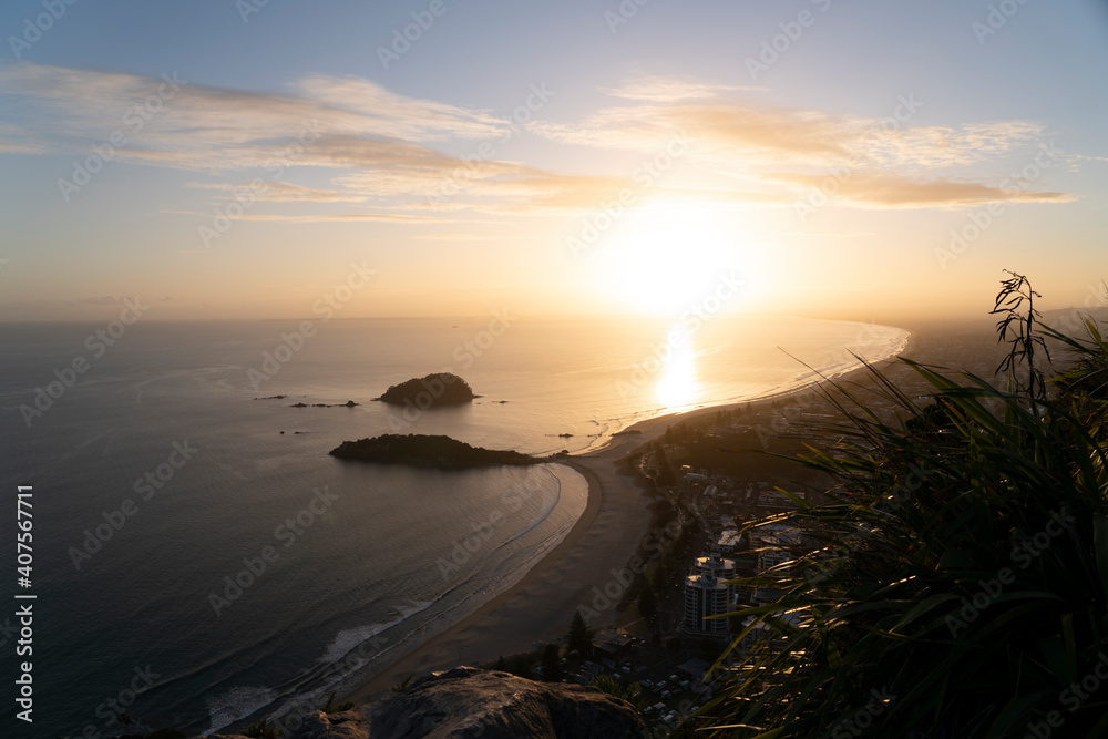 Sun on horizon illuminates long Mount Maunganui coast from summut of ...