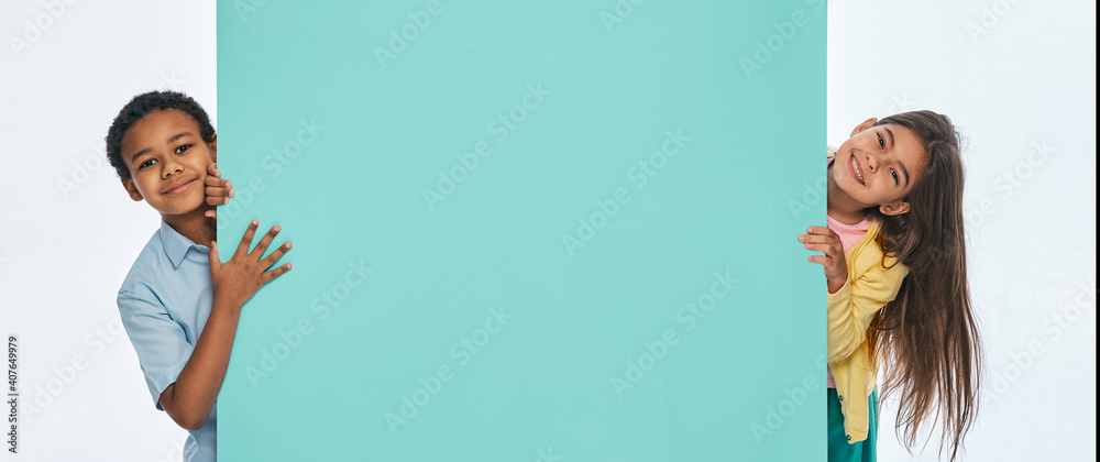 Multi-ethnic children peeking from behind an empty turquoise wall ...