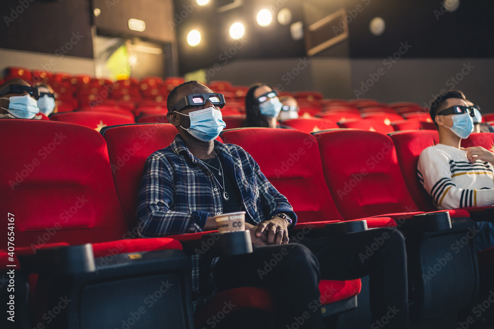 People sit in the cinema hall and watch a movie wearing medical masks ...
