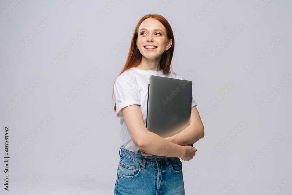 Smiling young woman student holding laptop computer and looking away on ...