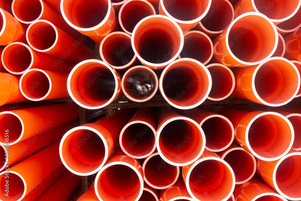 Stacked bright orange electrical conduit pipes end on making a pattern ...