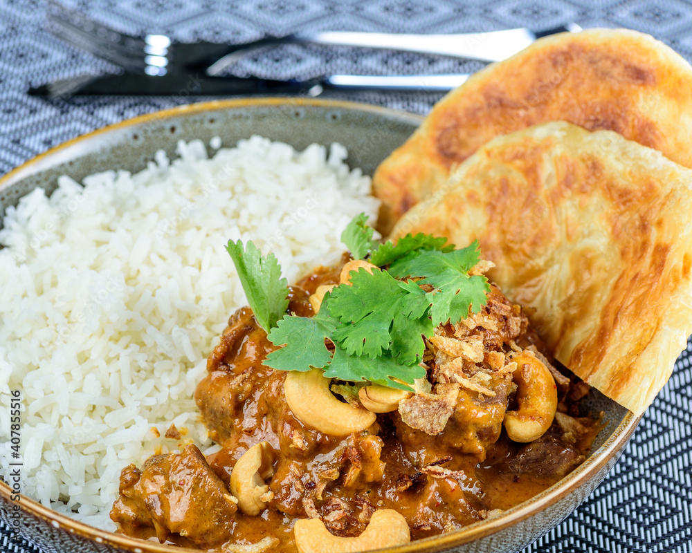 A serving of beef curry, with white rice and roti bread in a round bowl ...