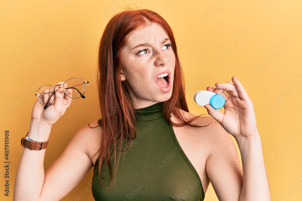 Young red head girl holding glasses and contact lenses angry and mad ...
