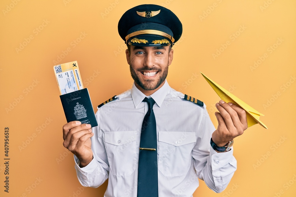 Handsome hispanic pilot man holding paper plane and passport smiling ...
