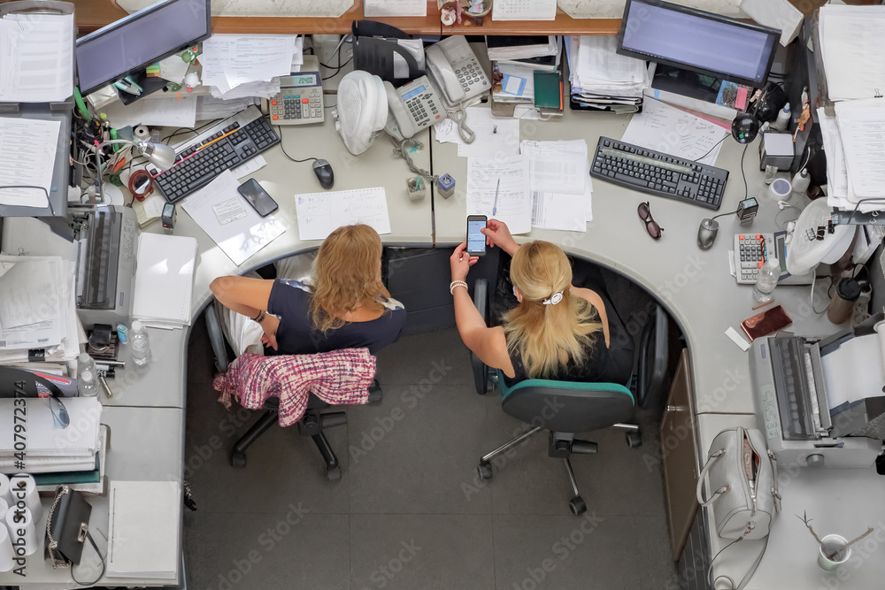 Two woman colleagues using smartphone in the office demonstrate message ...