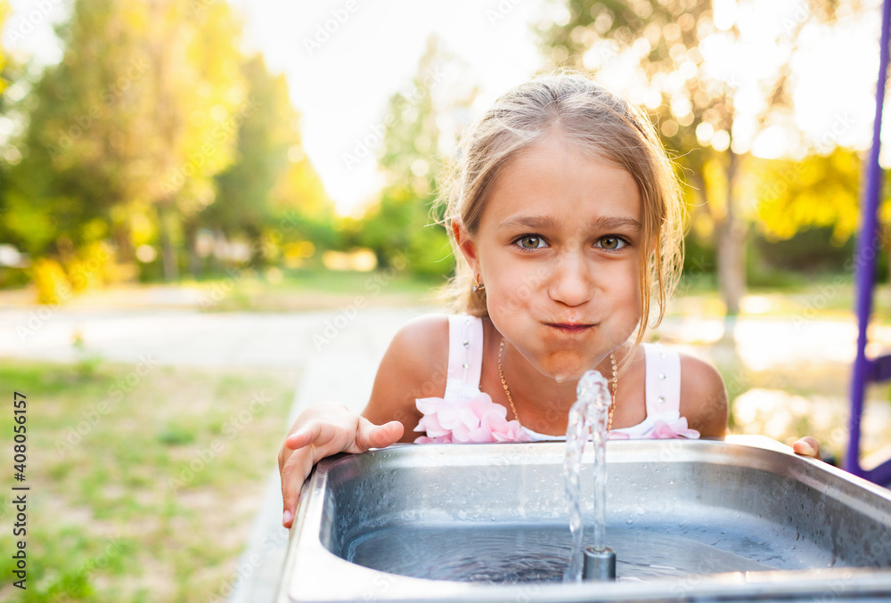 Cheerful wonderful girl drinks cool fresh water from a small fountain ...