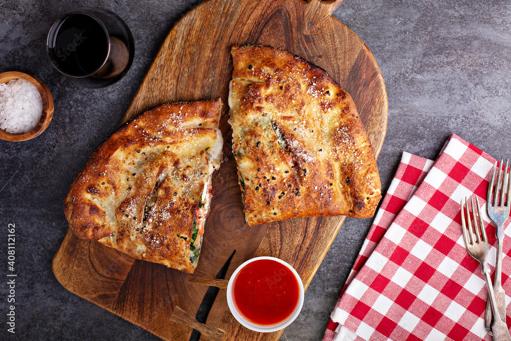 Poster Traditional calzone cut in half served with marinara sauce ...