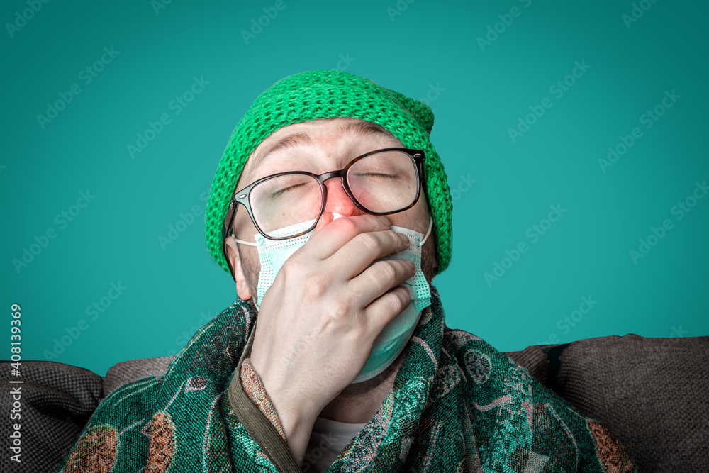 a man with a cold in glasses sits at home on the sofa wrapped in a ...