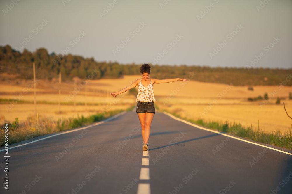 Young girl, walking in the middle of a lonely straight road, late in ...