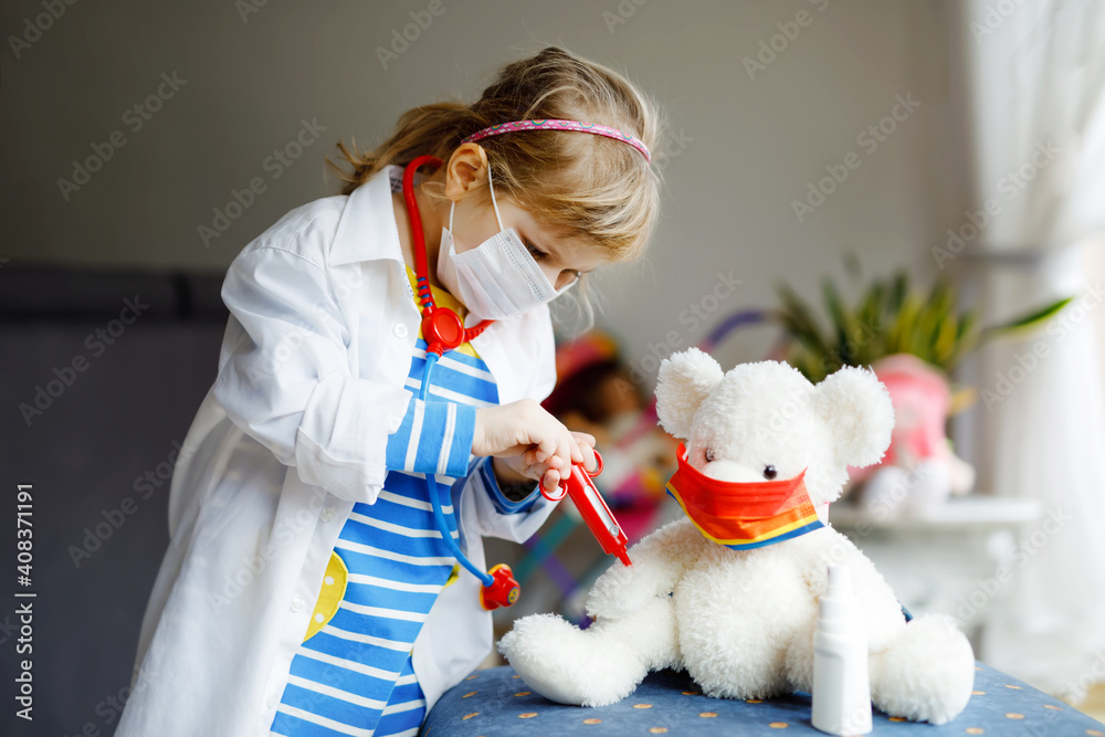 Little girl makes injection to teddy bear. Cute child with medical mask ...