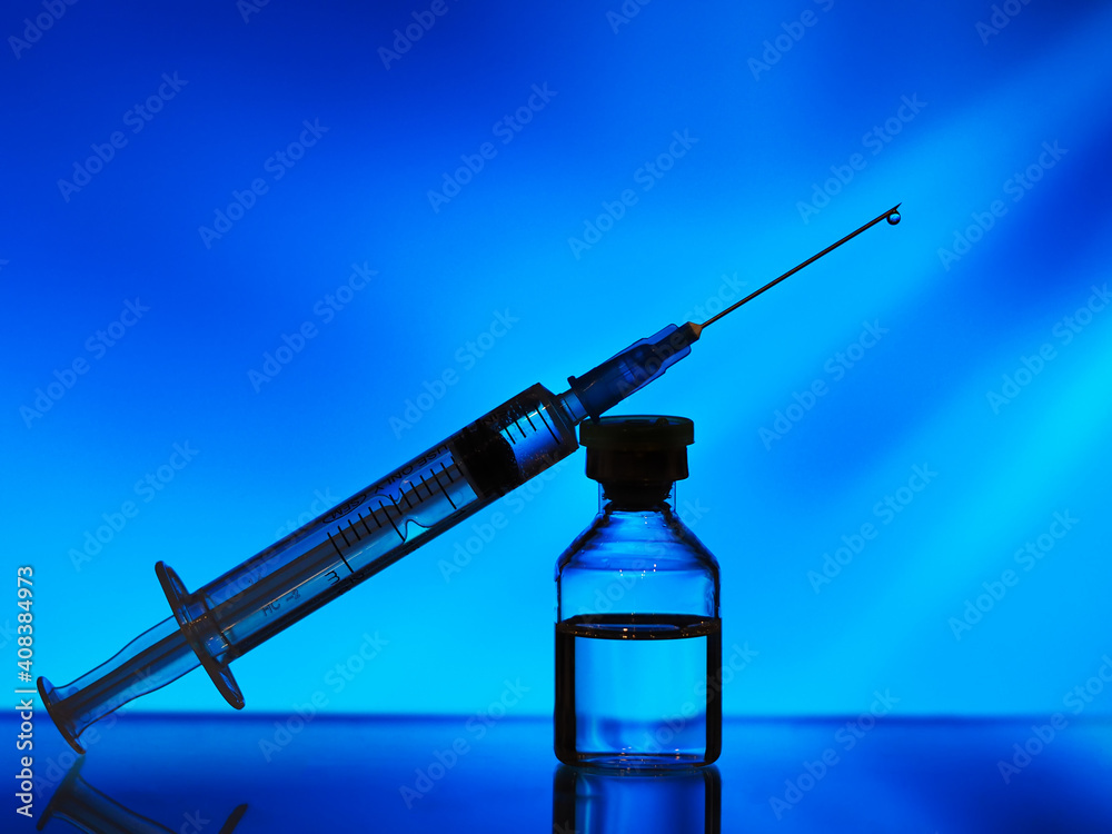 drop of transparent vaccine on the tip of a needle syringe, glass vials ...