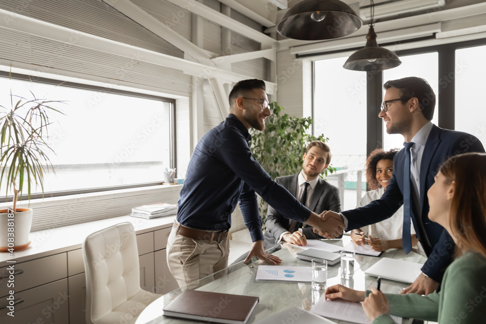 Diverse business partners shaking hand in modern boardroom after ...