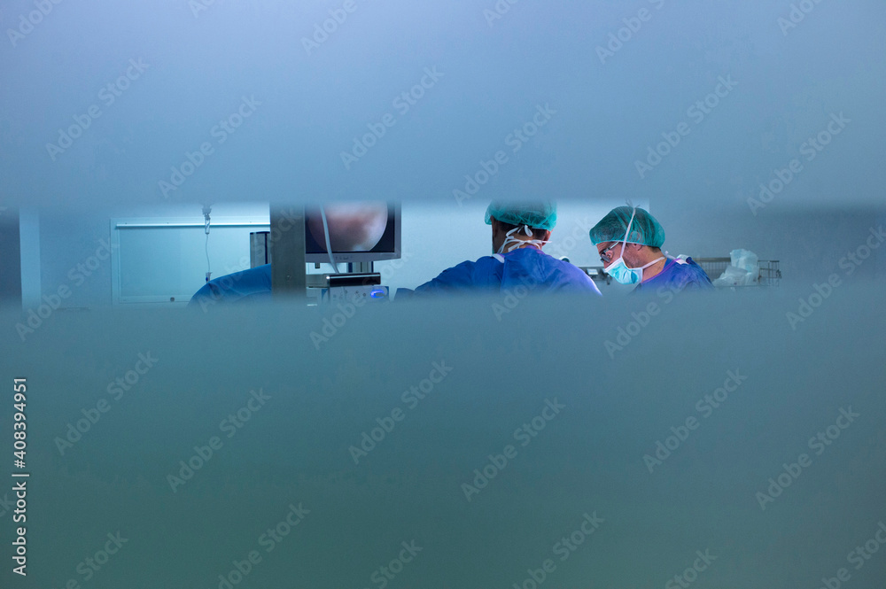 Male orthopedic surgeon seen through glass window while operating in ...