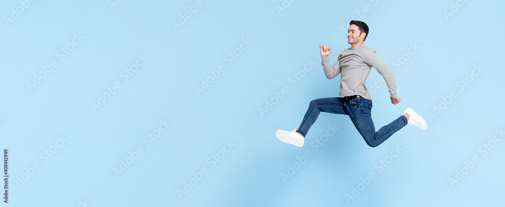 Smiling handsome man jumping in light blue color isolated studio ...