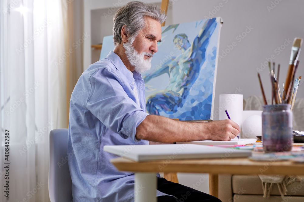 painter is drawing at home in light room, gray bearded man is creating ...