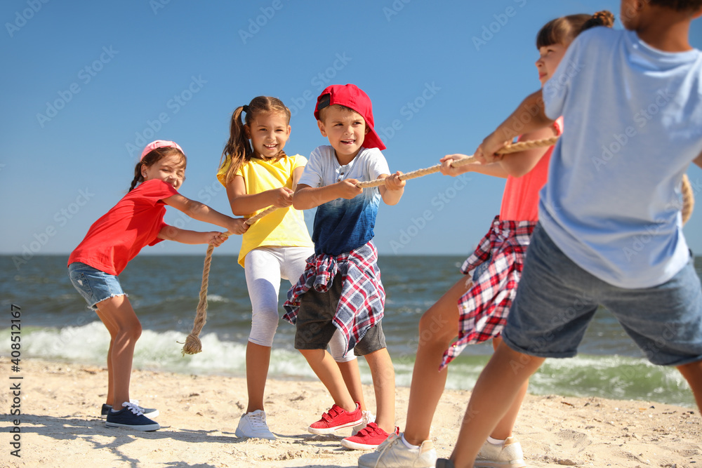 Cute children pulling rope during tug of war game on beach. Summer camp ...