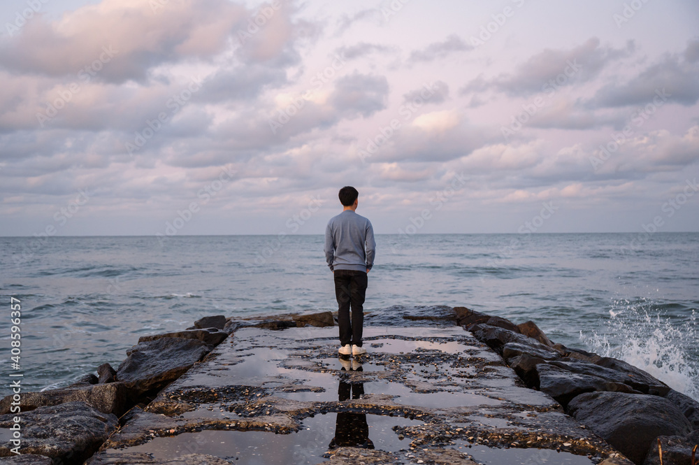 Rear of asian man standing on rocky pier with wave hitting in the ...