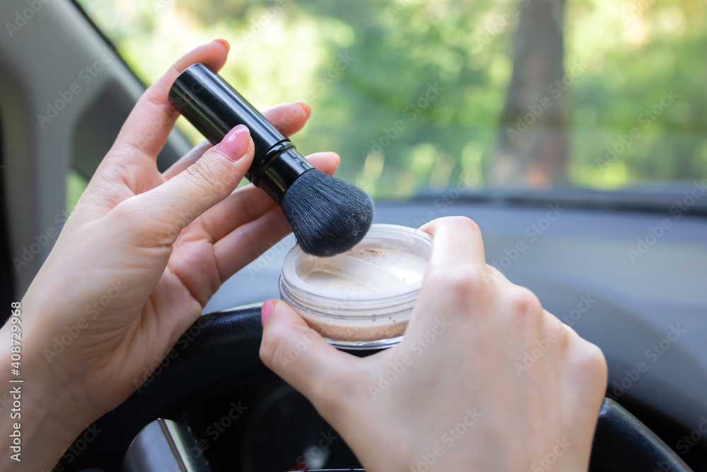 Woman is applying makeup in the car. Girl with face powder behind the ...
