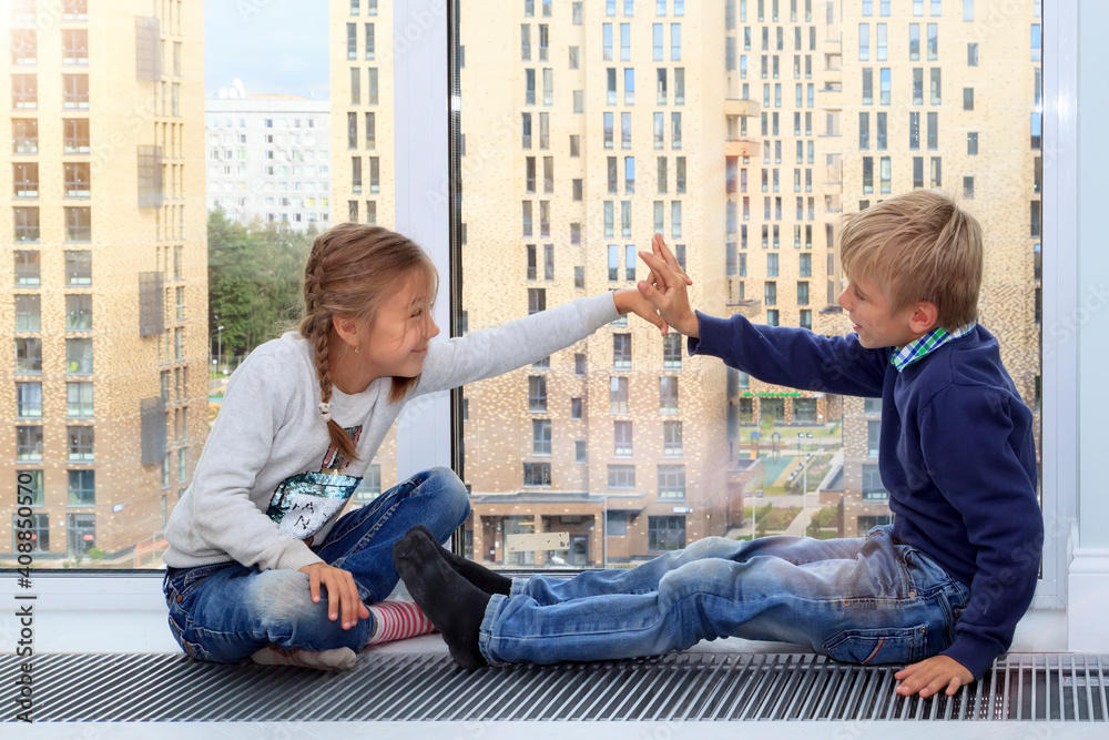 Girl gives five to boy. children sit on floor by window in new house ...
