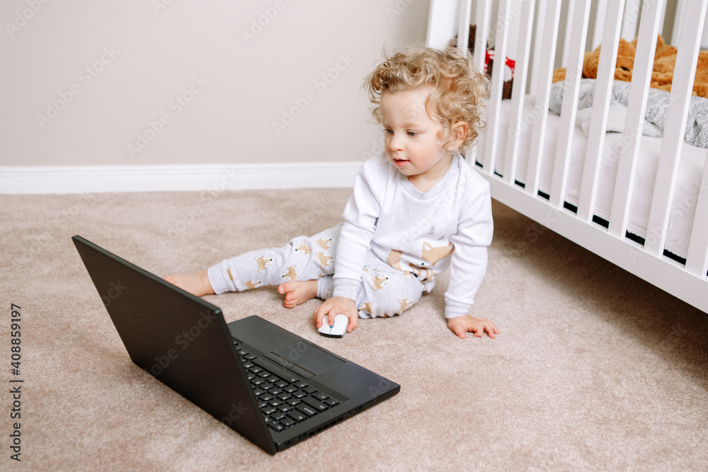 Cute blonde curly toddler baby boy working on laptop. Little kid child ...