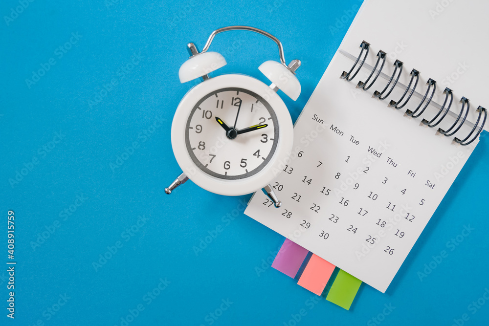 white analog alarm clock on white calendar with grunge blue background ...