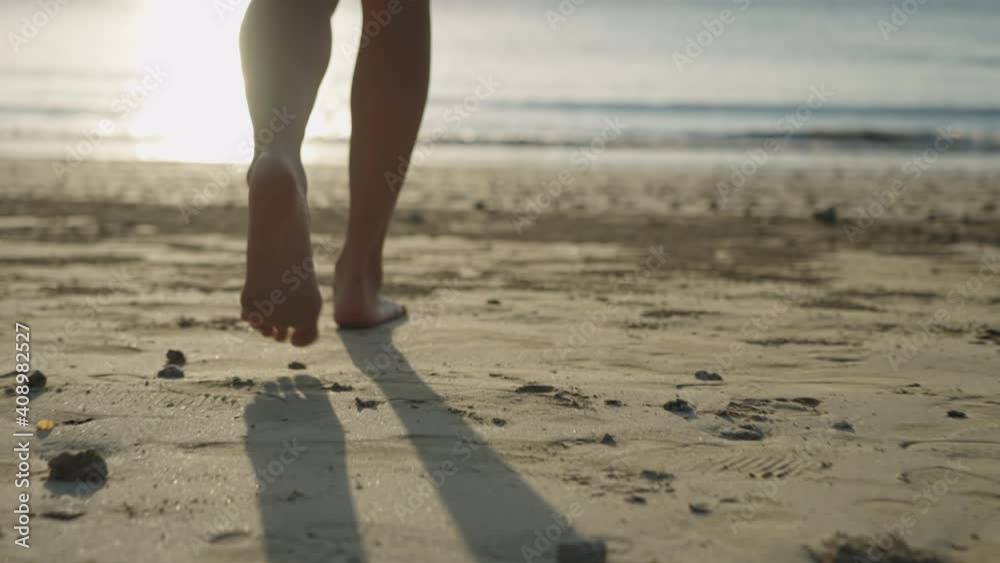 Female legs and feet walking down toward sea water waves on sandy beach ...