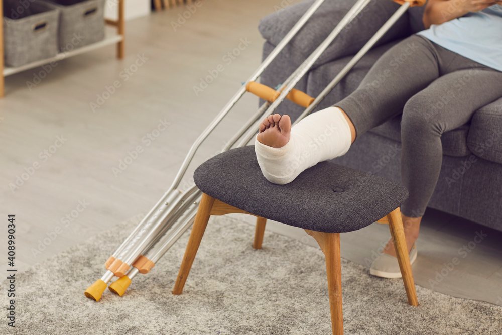 Close-up of females broken leg on stool in cast and metal crutches at ...