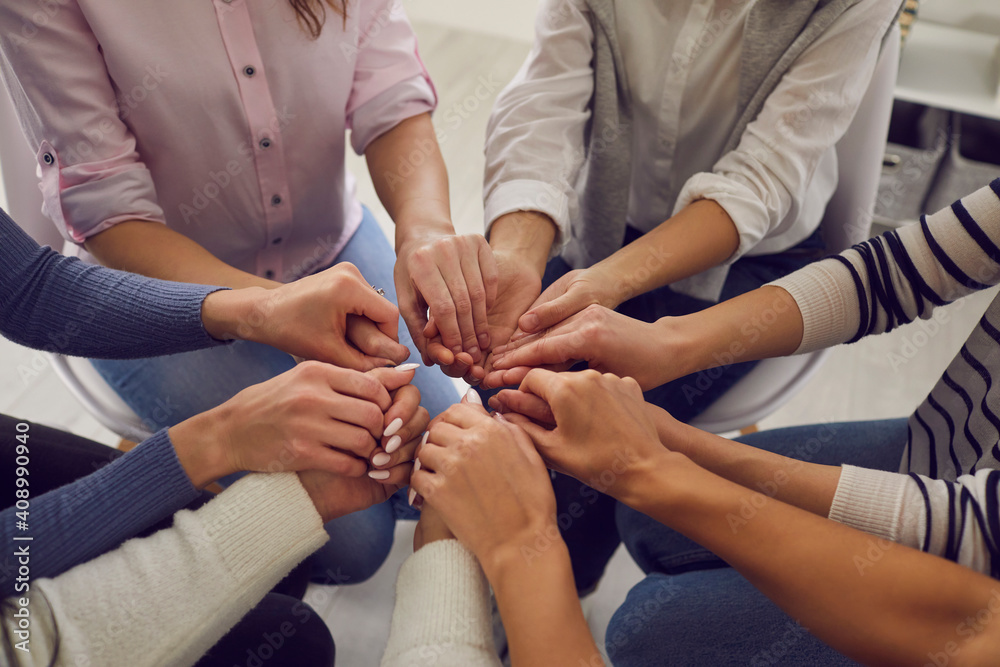 Team of young women sitting together and holding hands, demonstrating ...