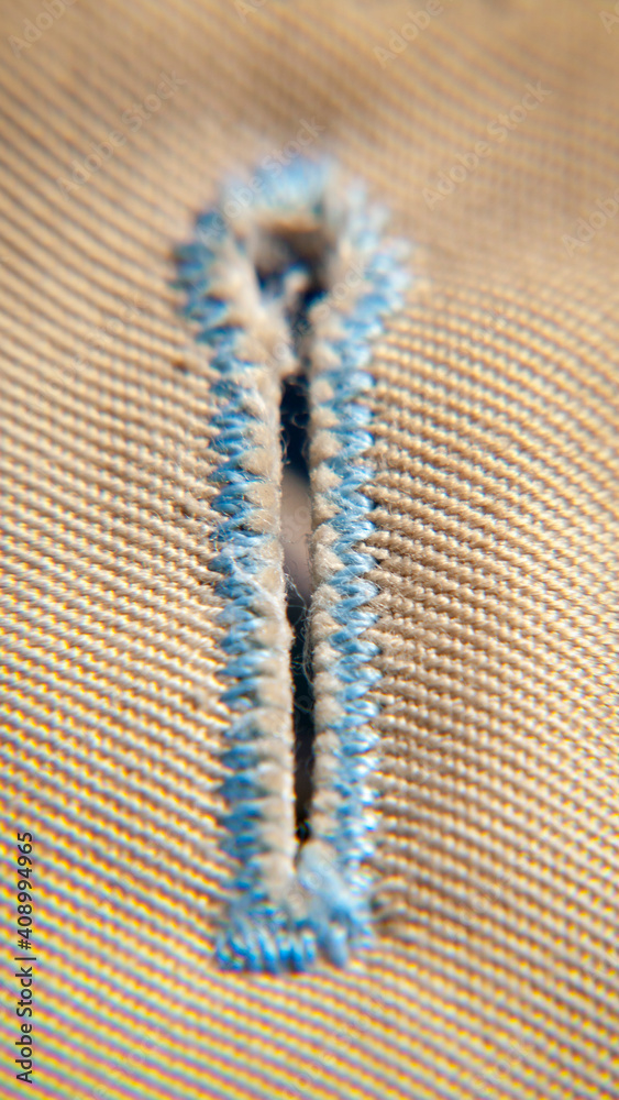 Ojal de botón con pespunte de hilo azul claro sobre tela de gabardina ...