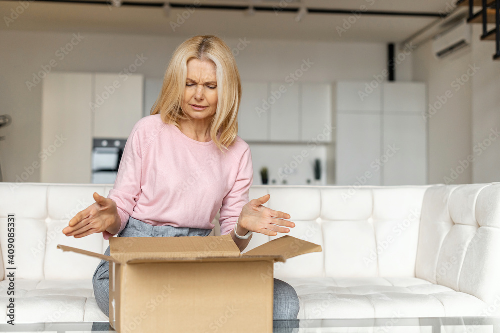 Disappointed middle-aged woman opens parcel carton box, unpacking it ...