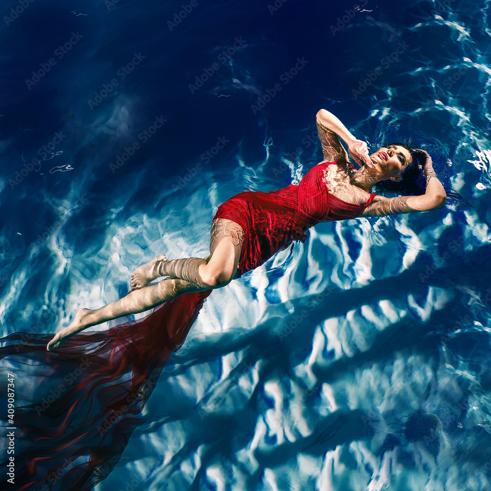 young woman in a red dress on the water. Girl swims in the water in a ...