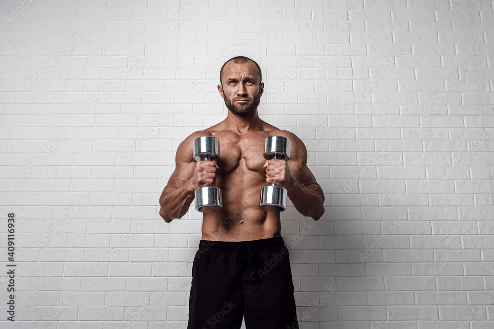 Bodybuilder doing exercises for biceps with a dumbbells against brick ...