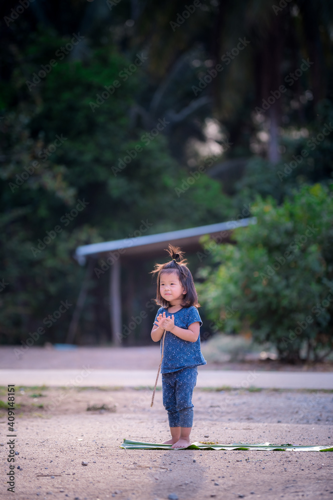 A 3 year old girl stands on a green banana leaf. She held a twig and tried to grasp her hand ...