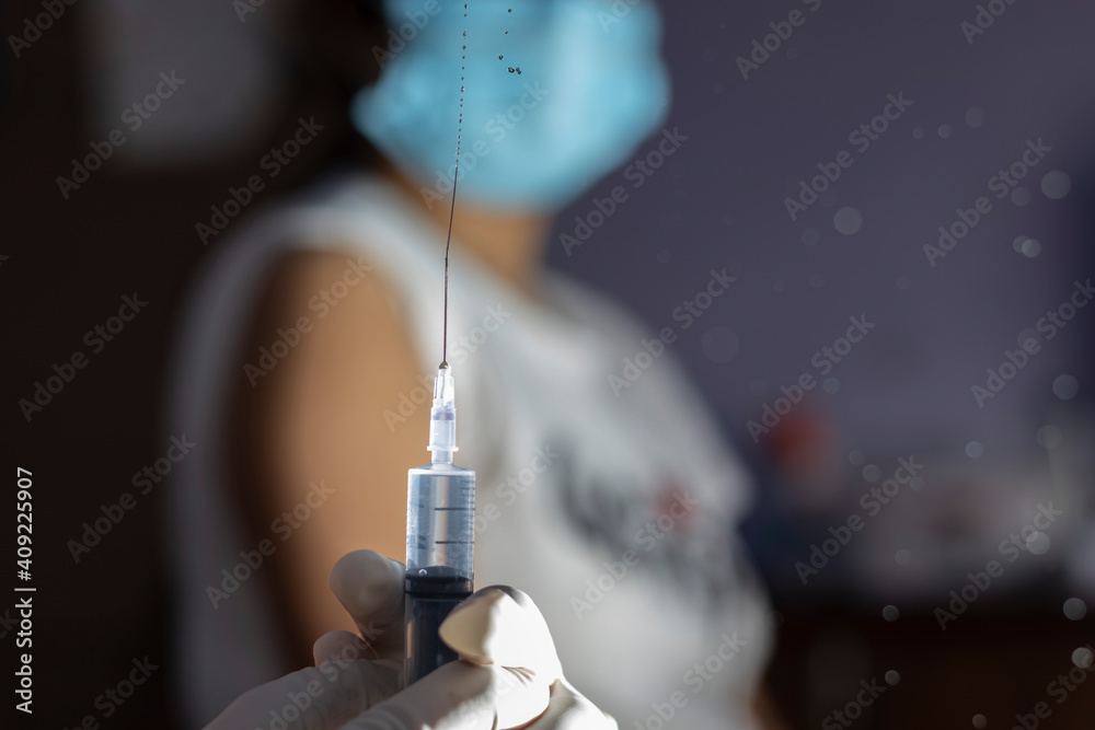 selective focus on an injection syringe in hands while a blurred woman ...