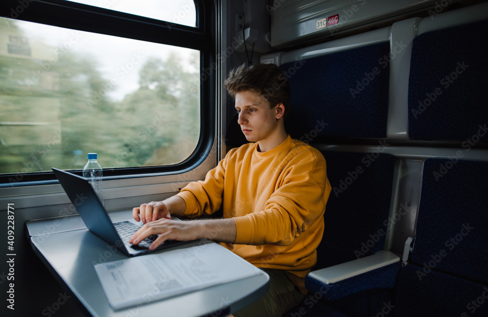 Handsome young freelancer man working on laptop in train sitting at the ...