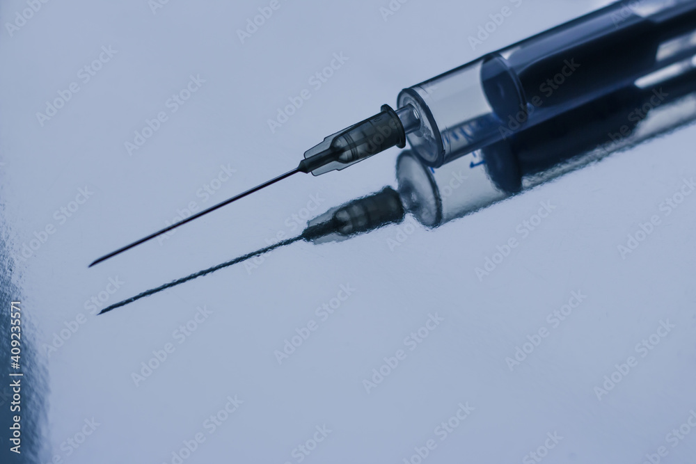 Medical syringe with a needle close-up on a mirrored reflective surface ...