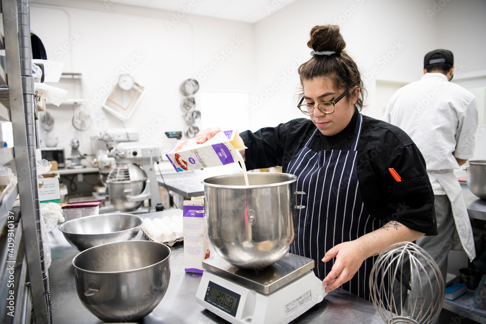 Female baker measuring heavy cream at scale in bakery kitchen Stock ...
