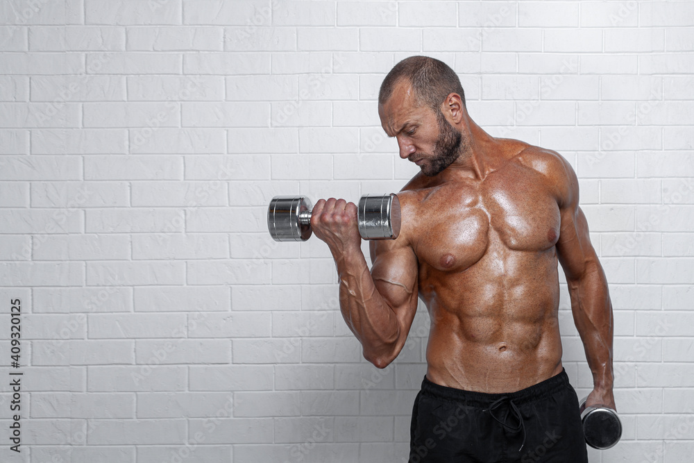 Bodybuilder doing exercises for biceps with a dumbbells against brick ...