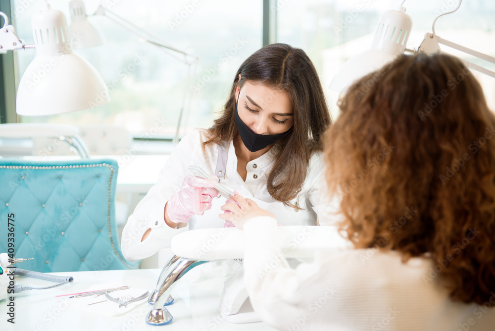 Professional manicure master in protective face mask using electric ...