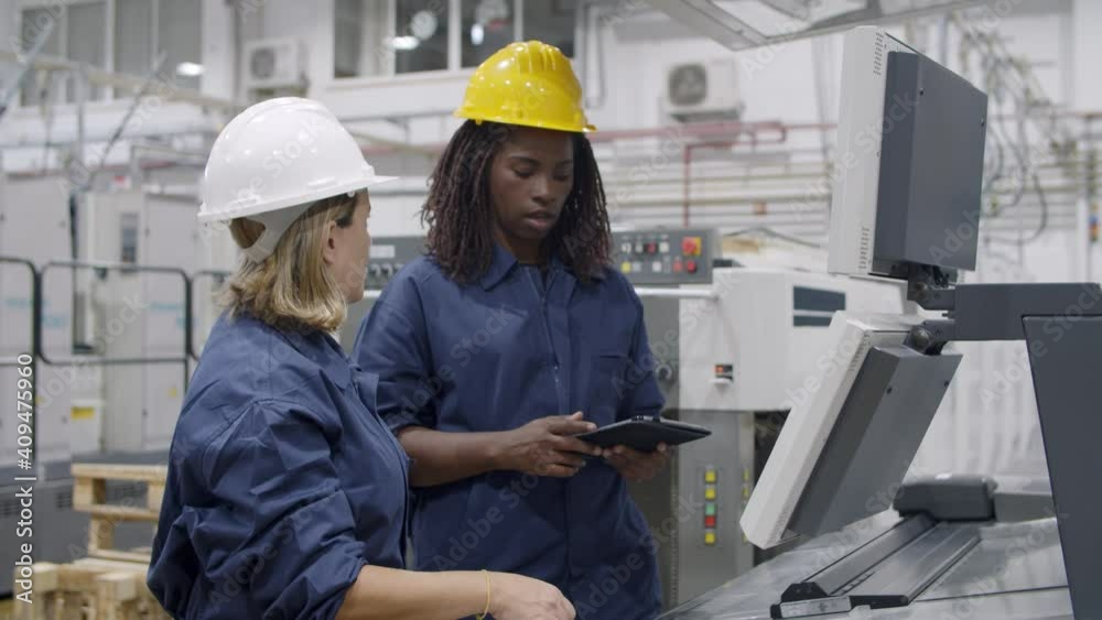 Female engineer teaching Black factory worker to operate new machine on ...