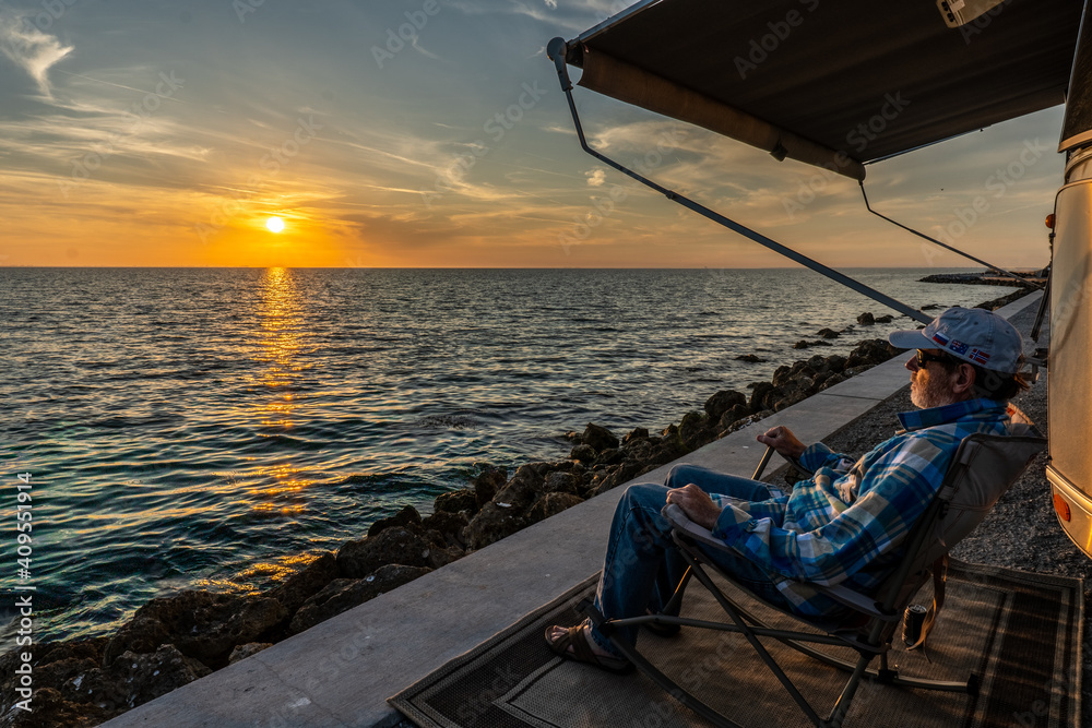 A man, person sitting on a rocking chair by a camper, enjoying the ...