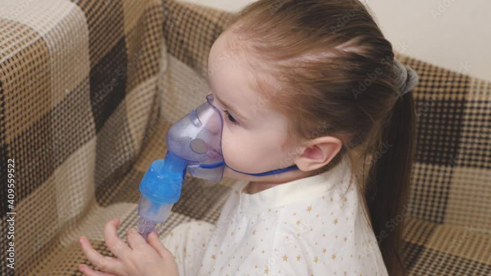 A cute baby in a mask is breathing through an inhaler. Home inhalation ...