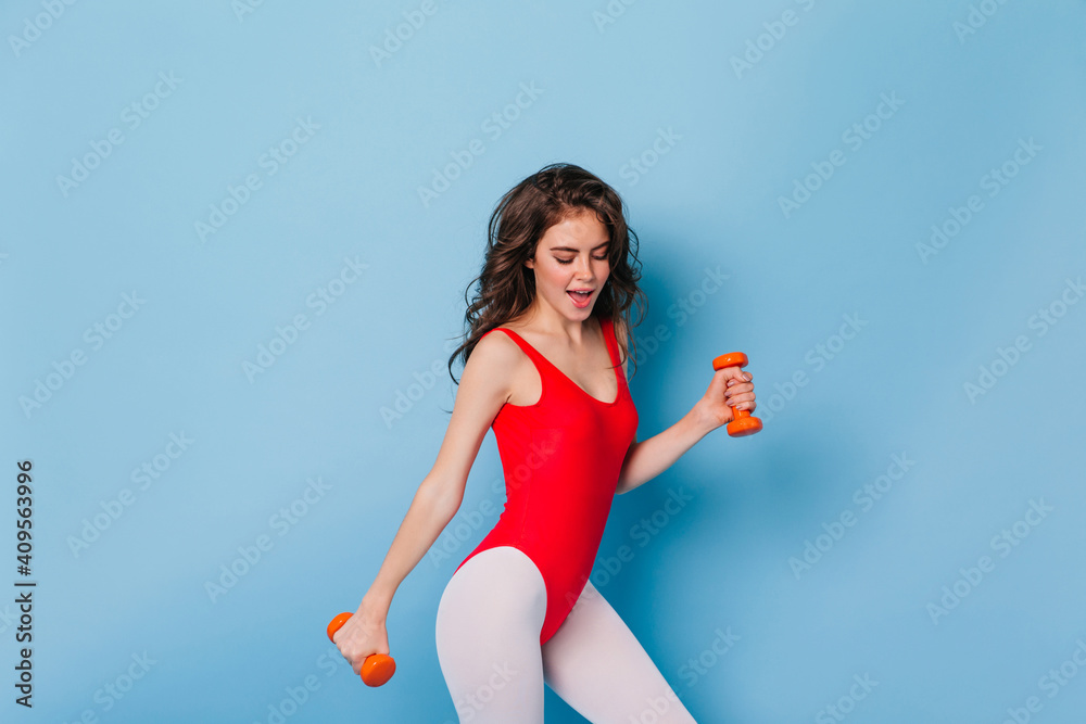 Young girl athlete in bodysuit in style of 80s does exercise for biceps ...