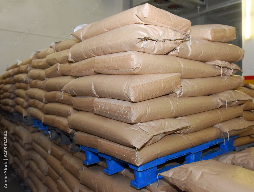 Large bags of construction material are stacked on pallets for loading ...