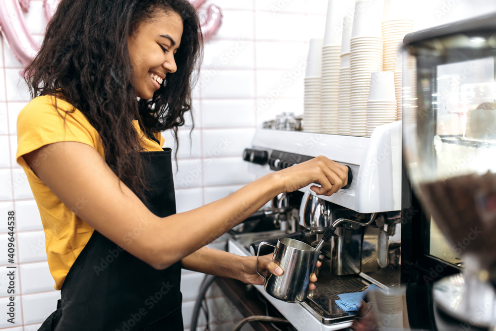 Smiling african american female barista wearing uniform makes coffee ...