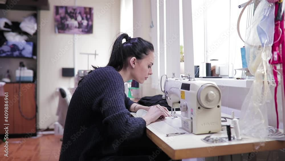 young woman sewing with professional machine at workshop. Dressmaker ...