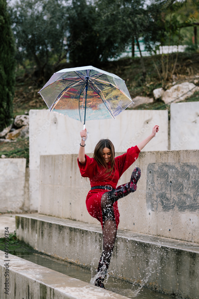 Foto de Young girl in a red dress, wellies and an umbrella enjoying and ...