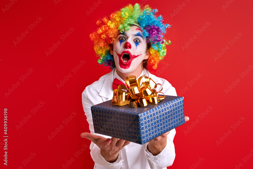funny clown holding gift box in hands posing at camera isolated over ...