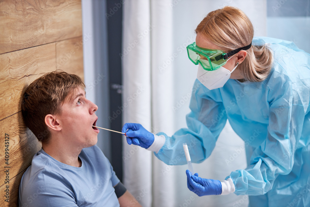 health professional in PPE suit introducing a nasal and throat swab to ...